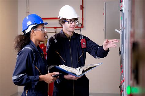 전기 젊은 여성과 남자 엔지니어는 유지 보수 캐비닛 시스템을 전기로 검사하고 공장 기술자 또는 전기 기술자 검사 전력 분배의 제어실에서 수동 책을 찾고 있습니다 전기공에