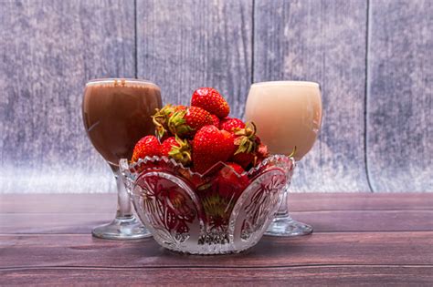 잘 익은 붉은 딸기와 칵테일 두 잔을 곁들인 크리스탈 꽃병이 나무 테이블 위에 서 있습니다 0명에 대한 스톡 사진 및 기타