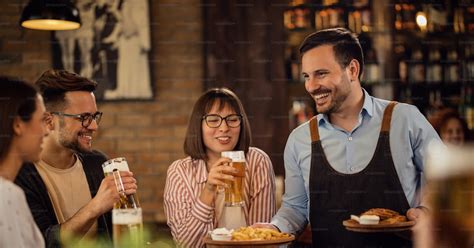 웨이터가 선술집에서 간식을 제공하는 동안 맥주를 마시는 행복한 친구들의 작은 그룹 사진 Unsplash의 맥주잔 이미지