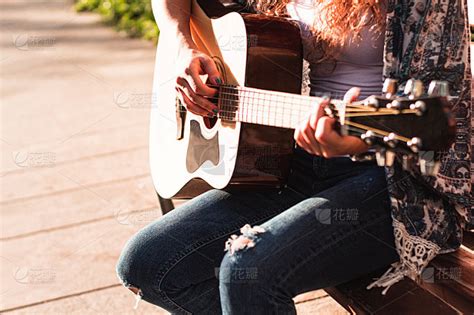 夕阳下，一个漂亮的女人坐在街道的长椅上弹吉他。有选择性的重点。