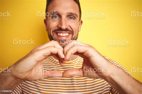 노란 고립 된 배경 위에 캐주얼 한 티셔츠를 입고 있는 젊은 잘생긴 남자의 가까이에서 하트 기호와 손으로 모양을 보여주는 사랑에 미소 로맨틱 한 개념 남자에 대한 스톡 사진
