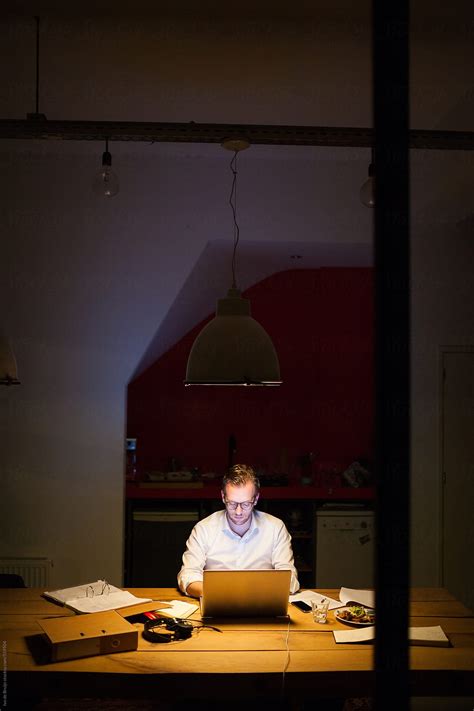 Young Man Working Overtime In A Dark Office Behind His Laptop By
