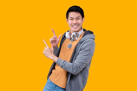 휴식 레저 종료 라이프 스타일 아시아 남성 성인 힙 스터 캐주얼 천 헤드폰 동작 자세 움직임 손 제스처 포인트 공기 복사 공간 쾌활 한 미소 스튜디오 촬영 노란색 배경 30