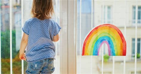 무지개가 그려진 창문을 통해 보고 있는 사랑스러운 유아 소녀 봉쇄 기간 동안 집에 머무르는 아이들을 위한 창의적인 게임 자가 격리 및 코로나바이러스 검역 개념 사진