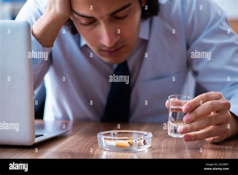The Male Employee Drinking Vodka And Smoking Cigarettes At Workplace