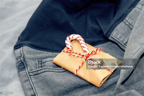 빨간색과 흰색 리본으로 묶인 두꺼운 노란색 크래프트 종이에 담긴 축제 선물 봉투는 어두운 바지에 크리스마스 사탕 지팡이 옆에 놓여 따뜻함과 휴일의 기쁨을 불러일으킵니다 갈색