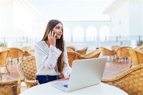 카페에서 전화 클라이언트 들과 얘기 하는 행복 한 프리랜서의 초상화 젊은 백인 여자 리조트에서 노트북 및 호출 파트너 테이블에 앉아 프리랜서 및 야외 비즈니스 개념 노트북에
