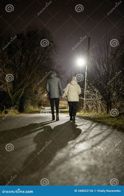 Two People Walking Together On A Quiet Street At Night Under A