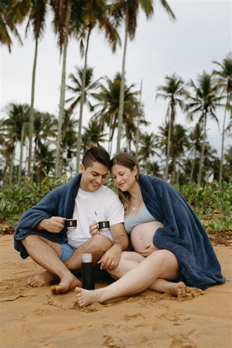 열대 해변에서 휴식을 취하는 임산부 커플 · 무료 스톡 사진