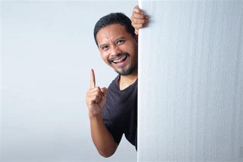 Premium Photo Happy Man Peeking Behind The Wall While Pointing Finger Up