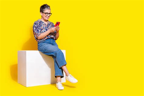 좋은 연금 수령자 여성의 전체 크기 사진 화이트 큐브 홀드 장치 착용 유행 화려한 옷차림 절연 통하고 노란색 배경 50 54세에 대한 스톡 사진 및 기타 이미지 Istock