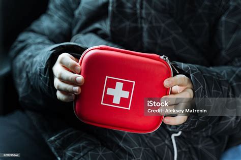 한 사람이 흰색 십자가 기호가 있는 밝은 빨간색 구급 상자를 조심스럽게 들고 있어 긴급한 상황에서 응급 의료 지원을 제공하는 데 중요한 역할을 강조하고 있습니다 건강관리와