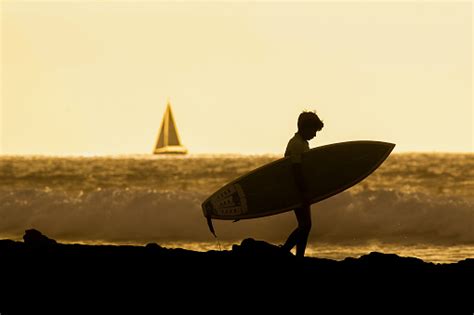 서퍼 젊은 남자는 파도와 함께 일몰 해변 바다에서 바다 해안 풍경에 자신의 손에 서핑 서 서 아름 다운 온화한 오렌지 빛 웨이크