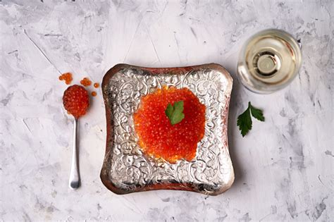 녹색이 있는 오래된 빈티지 금속 판에 있는 빨간 캐비어와 그 옆에 캐비어가 놓인 작은 숟가락 돌빛 배경에 가벼운 샴페인 한 잔이 있습니다 해산물 연어 캐비어 맨 위 보기