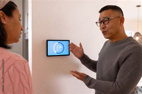 Explaining Smart Thermostat Asian Man Discussing Temperature Settings With Wife At Home Stock
