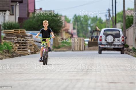 교외 오두막과 자동차 흐리게 배경에 햇볕이 잘 드는 빈 포장 거리를 따라 어린이 자전거를 타고 캐주얼 여름 의류에 귀여운 젊은 잘 생긴 금발 소년 어린이 게임 재미와 안전
