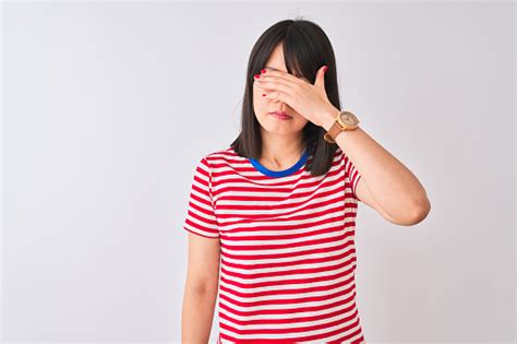 젊은 아름다운 중국 여성은 빨간색 줄무늬 티셔츠를 입고 고립 된 흰색 배경 위에 손으로 눈을 덮고 심각하고 슬픈 찾고 시력 숨기기 및 거부 개념 T 셔츠에 대한 스톡 사진