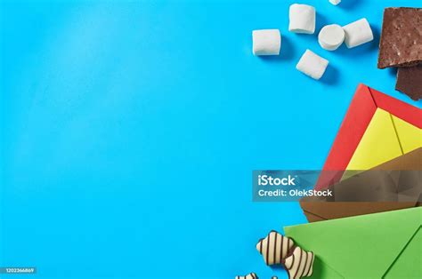 흩어진 과자 줄무늬 사탕 원통형 마시멜로 봉투 더미 근처의 깨진 초콜릿은 파란색 책상 위에 놓여 있습니다 사랑 편지 개념입니다 텍스트의 공백입니다 맨 위 보기 갈색에 대한