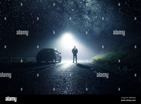 A Lone Car Parked On The Side Of The Road With A Hooded Figure On A