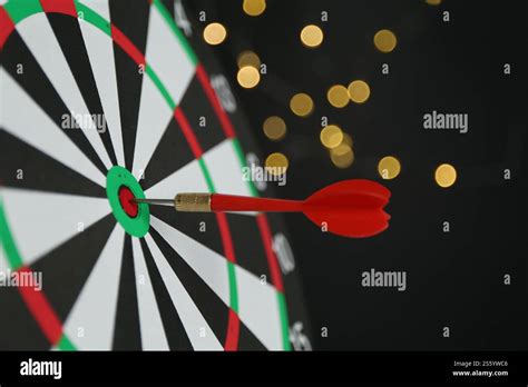 Red Arrow Hitting Target On Dart Board Against Black Background With Blurred Lights Closeup