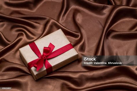 실크 같은 물결 모양의 갈색 패브릭 배경에 빨간 리본 크래프트 종이로 싸인 선물 상자 0명에 대한 스톡 사진 및 기타 이미지