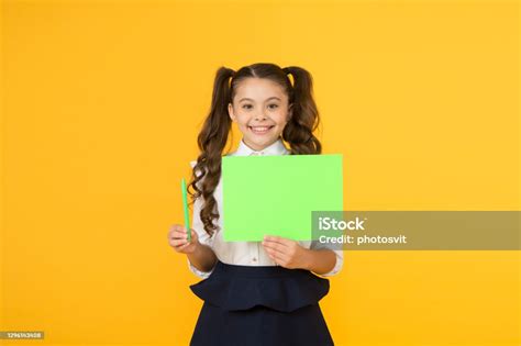 필기 펜을 가져옵니다 노란 배경에 작업을 작성하기위한 빈 종이 시트를 들고 어린 소녀 작은 아이는 정보를 작성하기 위한 녹색 포스터를 표시합니다 쓰기를 위한 빈 쇼 카드