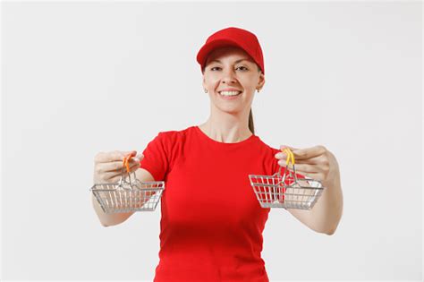 흰색 배경에 고립 된 빨간 유니폼에 배달 여자 여성 택배 또는 금속 식료품 슈퍼마켓에 쇼핑 바구니를 들고 모자 티셔츠 청바지에 딜러 광고에 대 한 공간을 복사 합니다