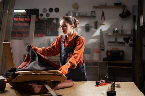 작업장에서 젊은 여성은 개조 과정에서 장인 정신과 세부 사항에 중점을 두고 새로운 모습을 제공하기 위해 안락 의자를 덮개를 씌우고 패브릭을 교체하여 오래된 가구를 복원합니다