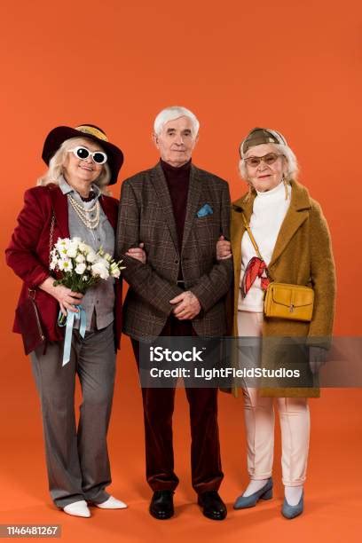 은퇴 한 남자와 오렌지 배경에 꽃을 들고 사이에 서 있는 세련 된 수석 여성 3 명에 대한 스톡 사진 및 기타 이미지 3 명
