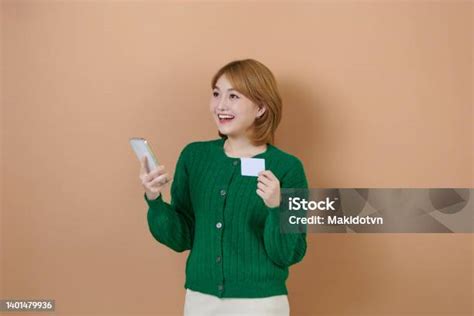 휴대 전화를 사용하는 즐거운 젊은 여성은 베이지 색 배경에 고립 된 신용 은행 카드를 들고 있습니다 30 34세에 대한 스톡 사진 및 기타 이미지 Istock