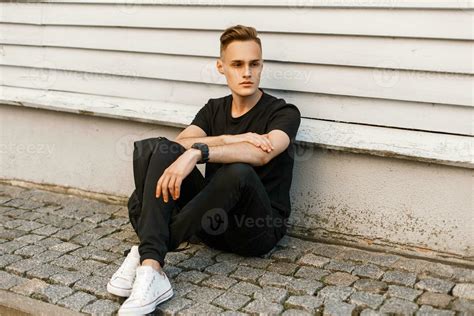 Beautiful Hipster Guy In Stylish Black Clothes And White Shoes Resting