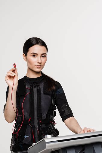 Ems 슈트를 입은 소녀는 전기 충격을 사용하여 흰색 배경에 근육을 자극하는 접촉기를 손에 들고 있습니다 전기 근육 자극 슈트에서 스포츠 훈련 18 19세에 대한 스톡 사진