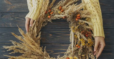 소박한 나무 테이블에 마른 풀 야생화 밀 열매가 있는 세련된 가을 소박한 화환을 들고 있는 손 휴일 워크샵 어두운 나무에 보헤미안 화환을 만드는 꽃집 사진