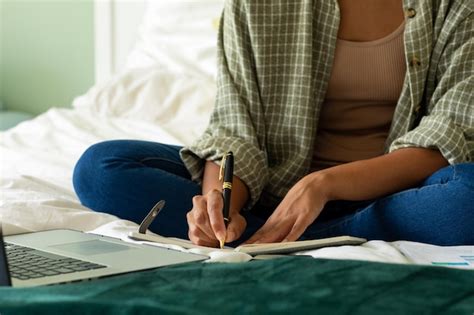 Premium Photo Mid Section Of Biracial Woman Taking Notes In Notebook And Using Laptop On Bed