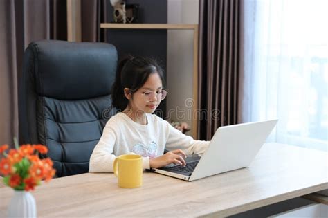 Young Asian Schoolgirl Is Doing Her Class Homework Assignment At Home Using Laptop Computer For