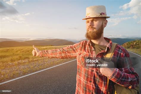 모자를 쓰고 배낭을 들고 산의 교외 아스팔트 도로를 따라 걷는 세련된 맨발의 수염 남성 히치하이커 여행자 거지에 대한 스톡 사진 및 기타 이미지 Istock