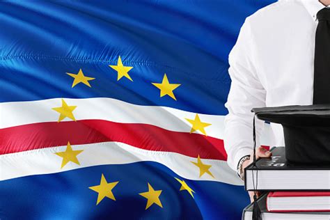 성공적인 학생 교육 개념입니다 케이프 베르데 국기 배경 위에 책과 졸업 모자를 들고 교사 교육 관련 직업에 대한 스톡 사진 및