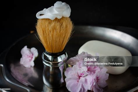 상단에 Foarm이 있는 면도 브러쉬와 부드러운 분홍색 의 제라늄 꽃과 검은 색 배경의 세강강철 꽃병 옆면에 흰색 비누 남성용