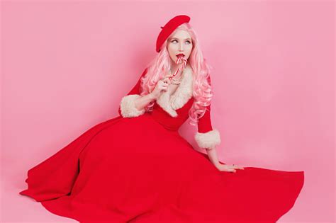 분홍색 배경에 모자에 빨간 크리스마스 드레스에 여자입니다 아름다운 산타 소녀 핥는 롤리팝 새해 컨셉입니다 긴 머리와 아름 다운