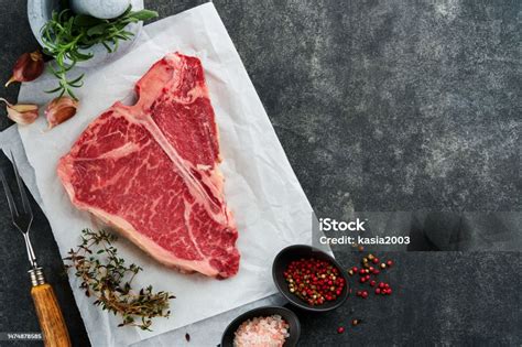 두꺼운 생 티본 스테이크 드라이 에이징 생 티본 또는 포터하우스 쇠고기 고기 양피지에 스테이크어두운 배경에 허브와 소금이