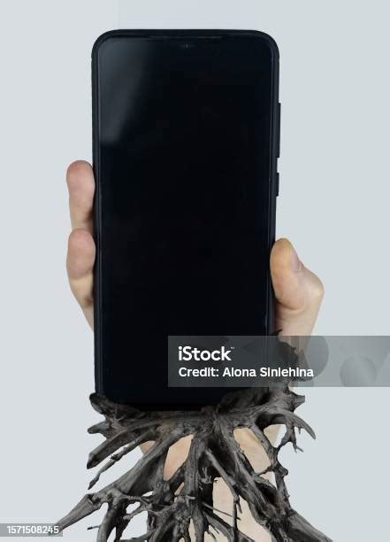 남자는 손에 스마트 폰을 들고 뿌리가 빠져 나와 손을 파고 든다 스마트폰 중독의 컨셉 샷 정상적인 삶을 살 수있는 능력의 상실