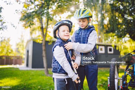 두 아이 오래 된 소년과 동생은 수리 자전거를 학습 두 남자 형제에 헬멧 및 단일 의류 사용 펌프 도구 및 펌프 공기 자전거 바퀴 공원에서 집의 배경 가족에 대한 스톡 사진