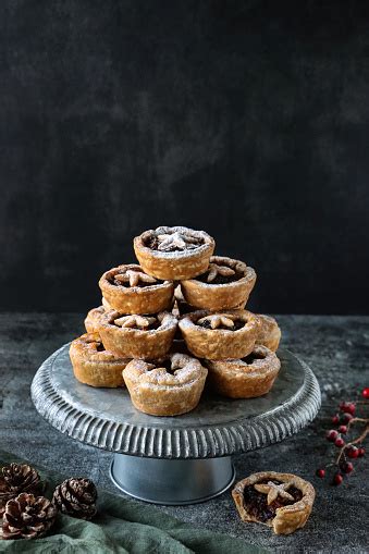 배치 홈메이드 다진 파이 달콤한 다진 고기로 채워진 바삭바삭한 패스트리의 축제 크리스마스 디저트 아이싱 설탕 금속 케이크 스탠드 모슬린 소나무 콘 빨간 열매 검은 배경