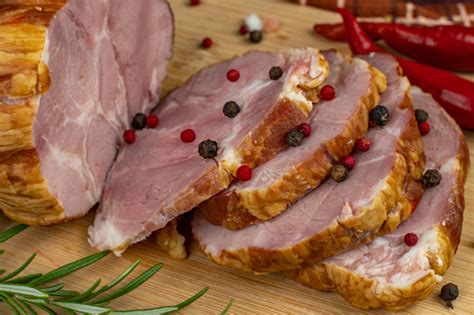 나무 도마에 육즙이 많은 돼지 고기 햄을 얇게 썬 조각 그 옆에는 조각 칼 멀티 컬러 피망 완두콩 붉은 고추 및 바질이 있습니다 클로즈업 맛있는 육류 제품의 개념 가정