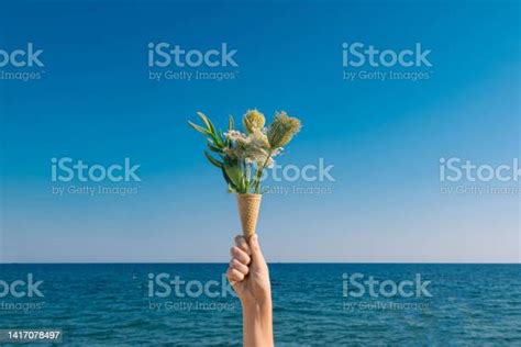 바다와 푸른 하늘로 만든 배경에 야생화가 달린 아이스크림 콘을 들고 있는 소녀의 손 자연 배너 또는 편집 또는 카드의 여름 휴가를위한 최소한의 개념 0명에 대한 스톡 사진