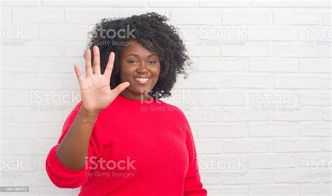젊은 아프리카계 미국인 플러스 크기 여자 및 손가락으로 가리키는 흰색 벽돌 벽을 통해 자신감과 행복 미소 하는 동안 5 번 가리키기에 대한 스톡 사진 및 기타 이미지