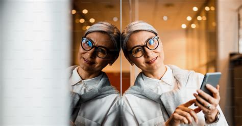 세련된 옷을 입은 긍정적인 성인 여성이 거울에 머리를 기대고 스마트폰을 들고 있다 사진 Unsplash의 숙녀 1명만 이미지