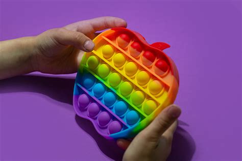 코카서스 소녀는 감각 안티 스트레스 멀티 컬러 팝 사과 모양 장난감에서 재생합니다 보라색 배경에 어린이와 성인을위한 다채로운 안티 응력 실리콘 센서 장난감 감각 지각에 대한