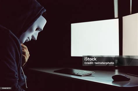 Masked Hacker Under Hood Using Computer To Hack Into System And Trying