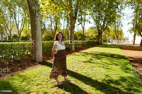젊고 행복하고 아름다운 아시아 한국 여성이 임신 한 도시 공원에서 야외에서 행복하고 쾌활한 포즈를 취하고 임신과 출산 개념에 미소를 짓는 배꼽을 보여줍니다 30 34세에